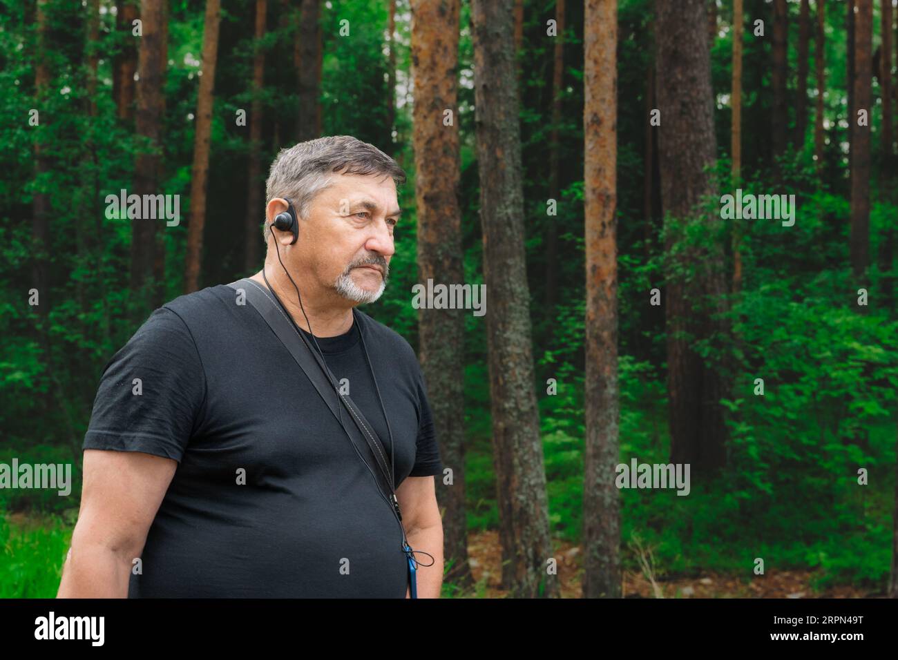 Portrait of a man in his 70s with a radio guide earpiece in the woods ...