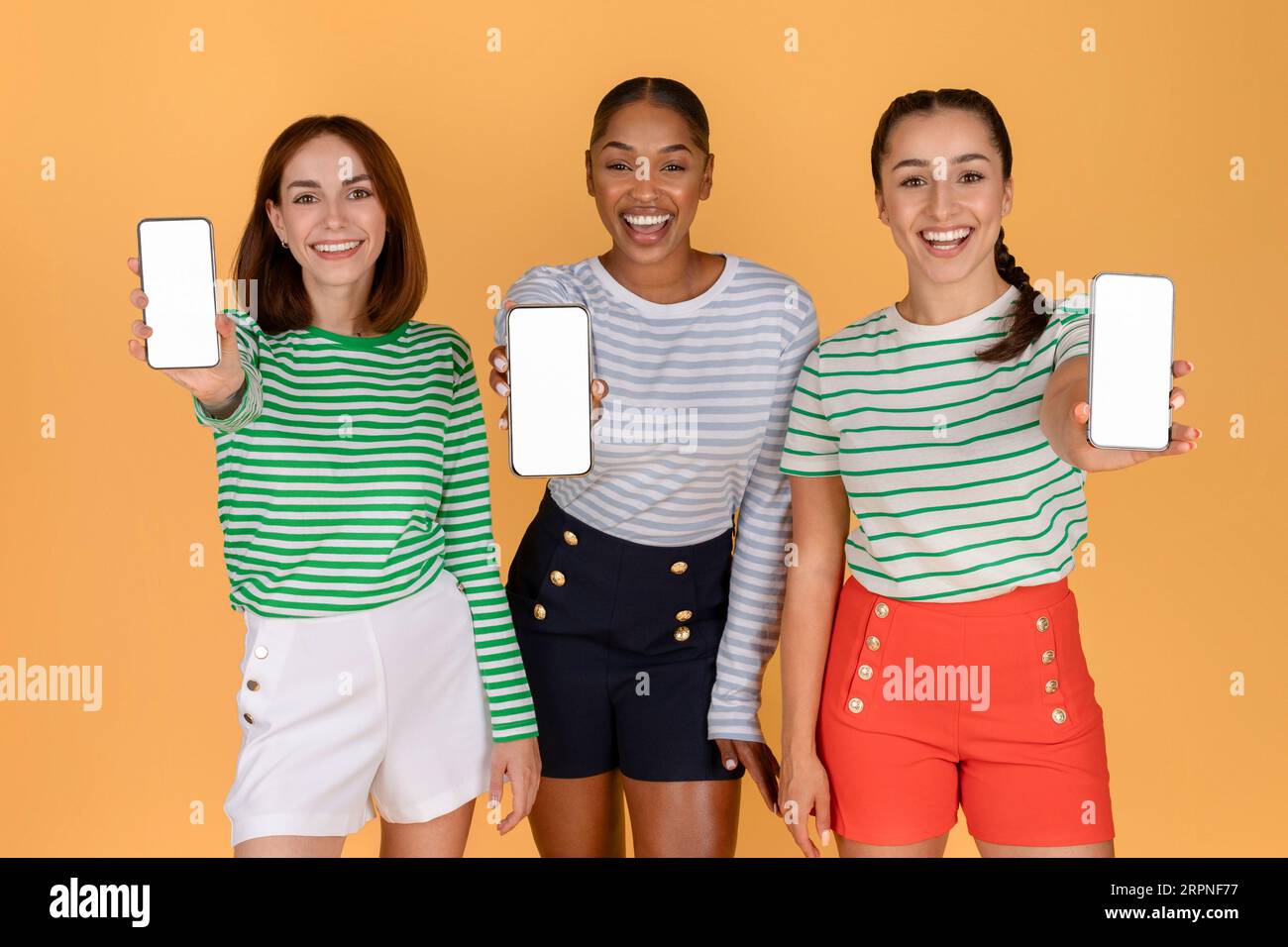 Happy multiethnic young women showing cell phones with blank screen ...