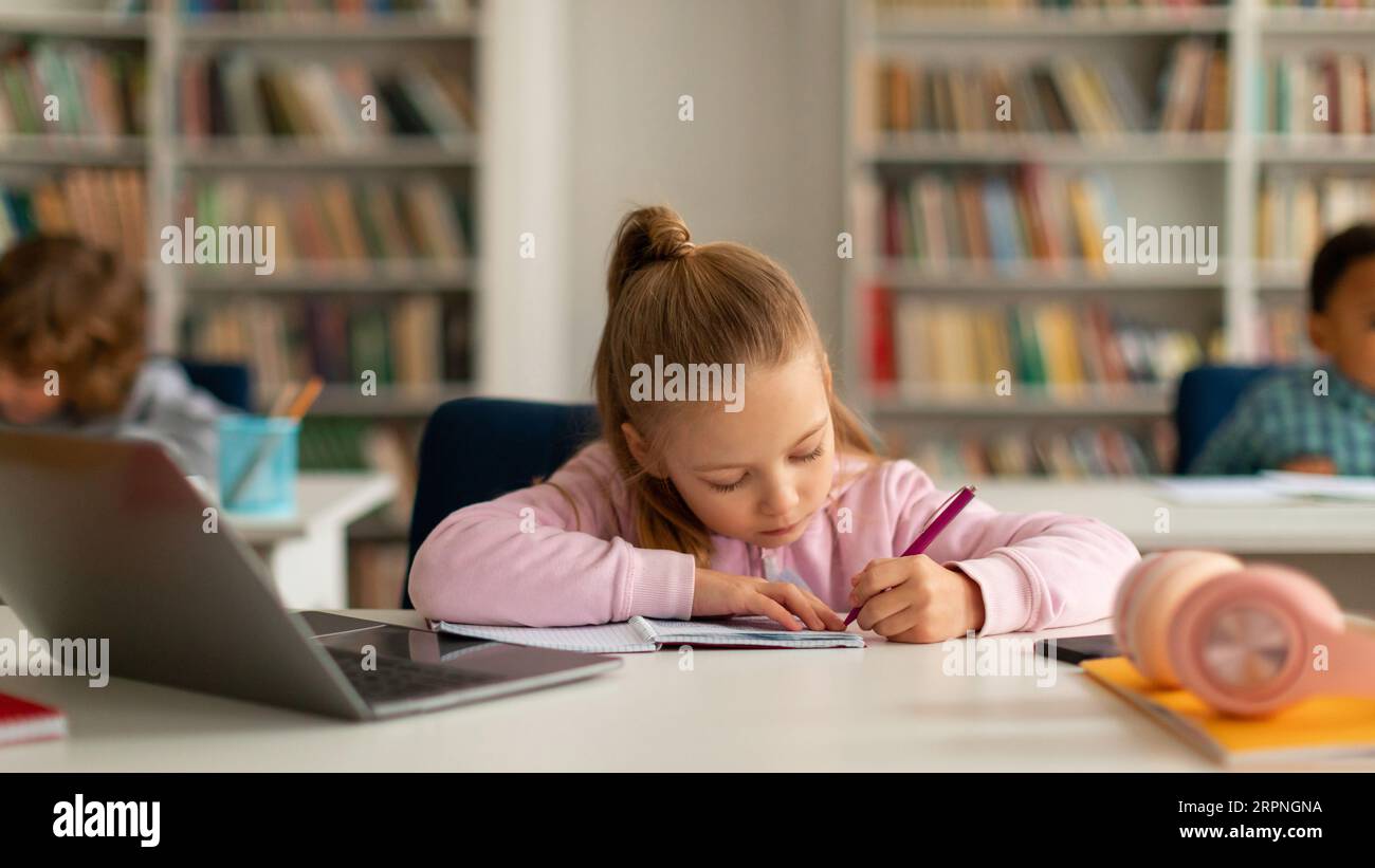 Smart schoolgirl taking notes while e-learning on laptop computer ...
