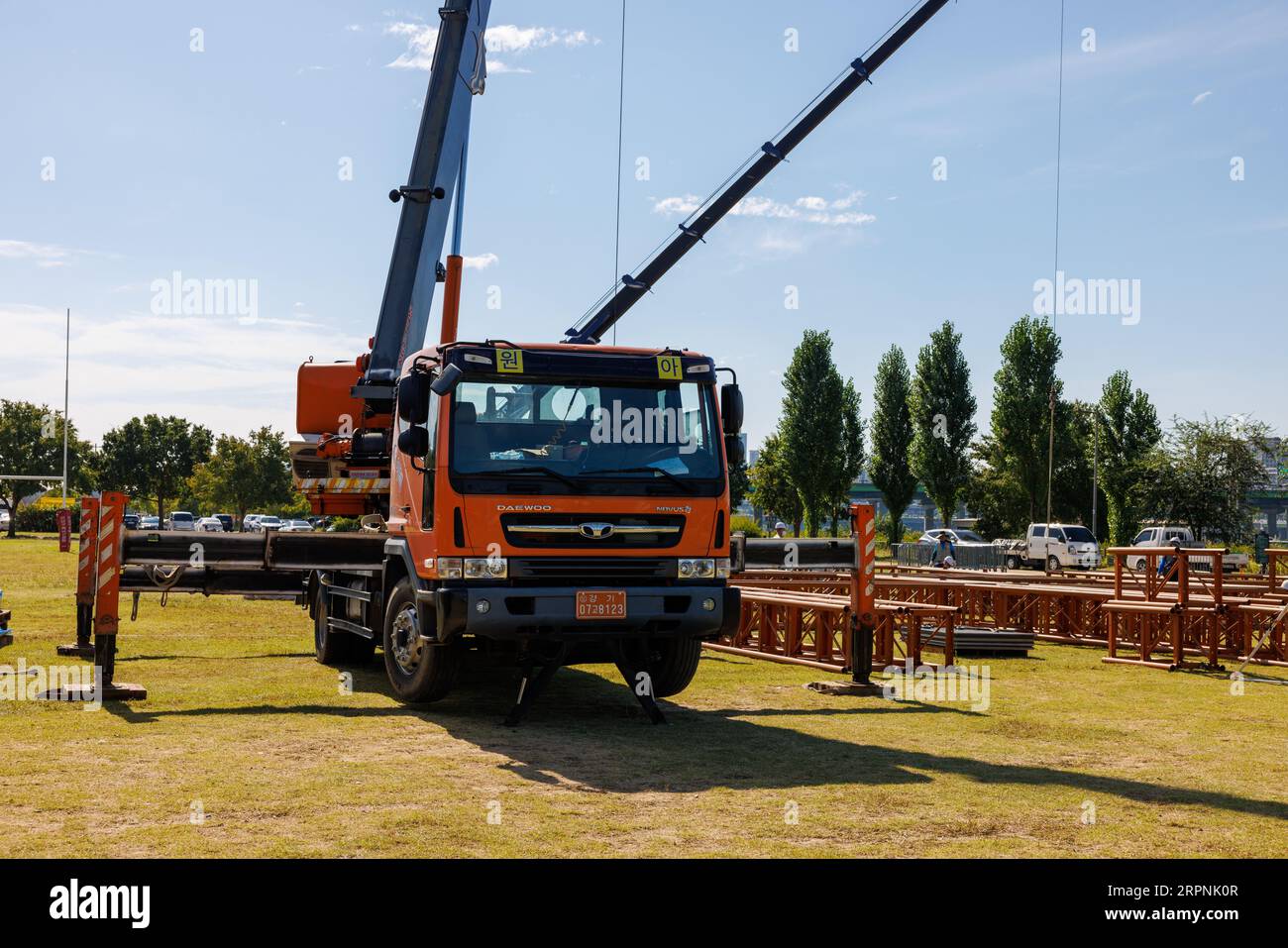 An orange crane is lifting a metal scaffolding to build a stage for a ...