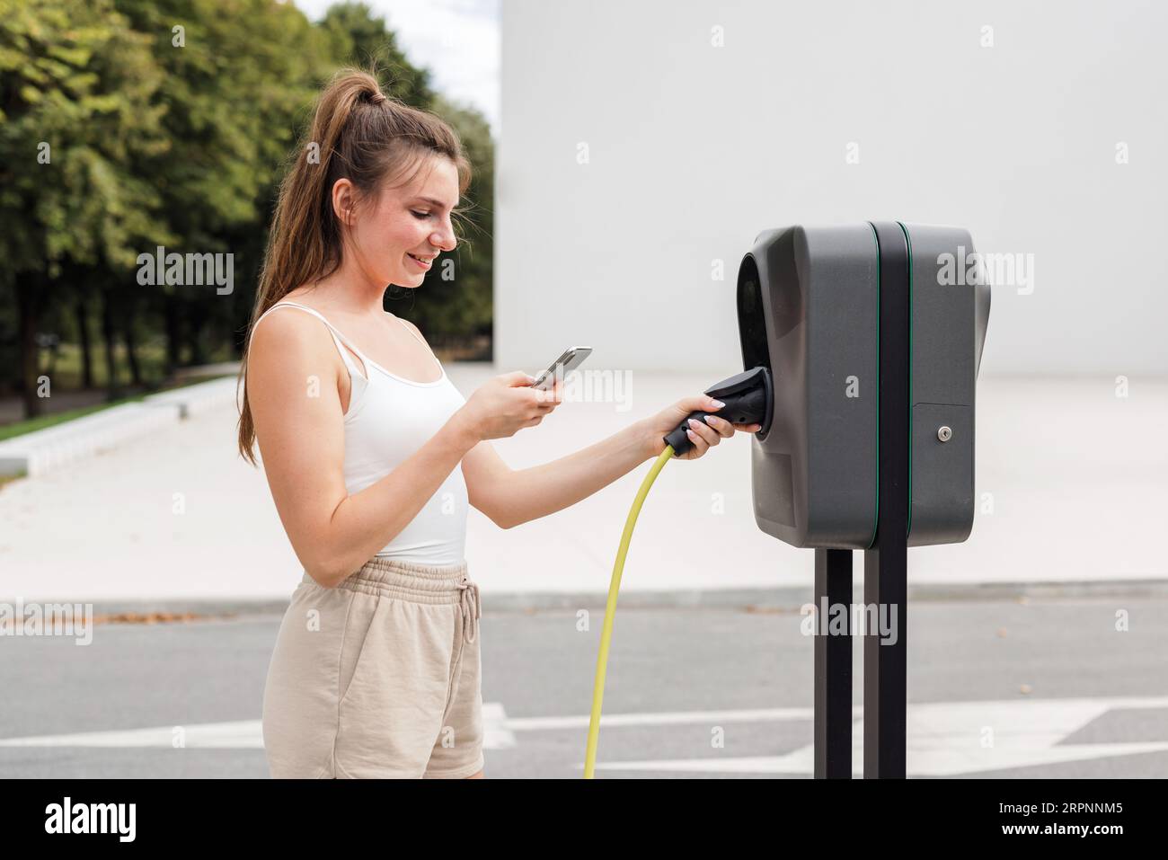 Beautiful girl plugging a cable charger into her parked black electric ...