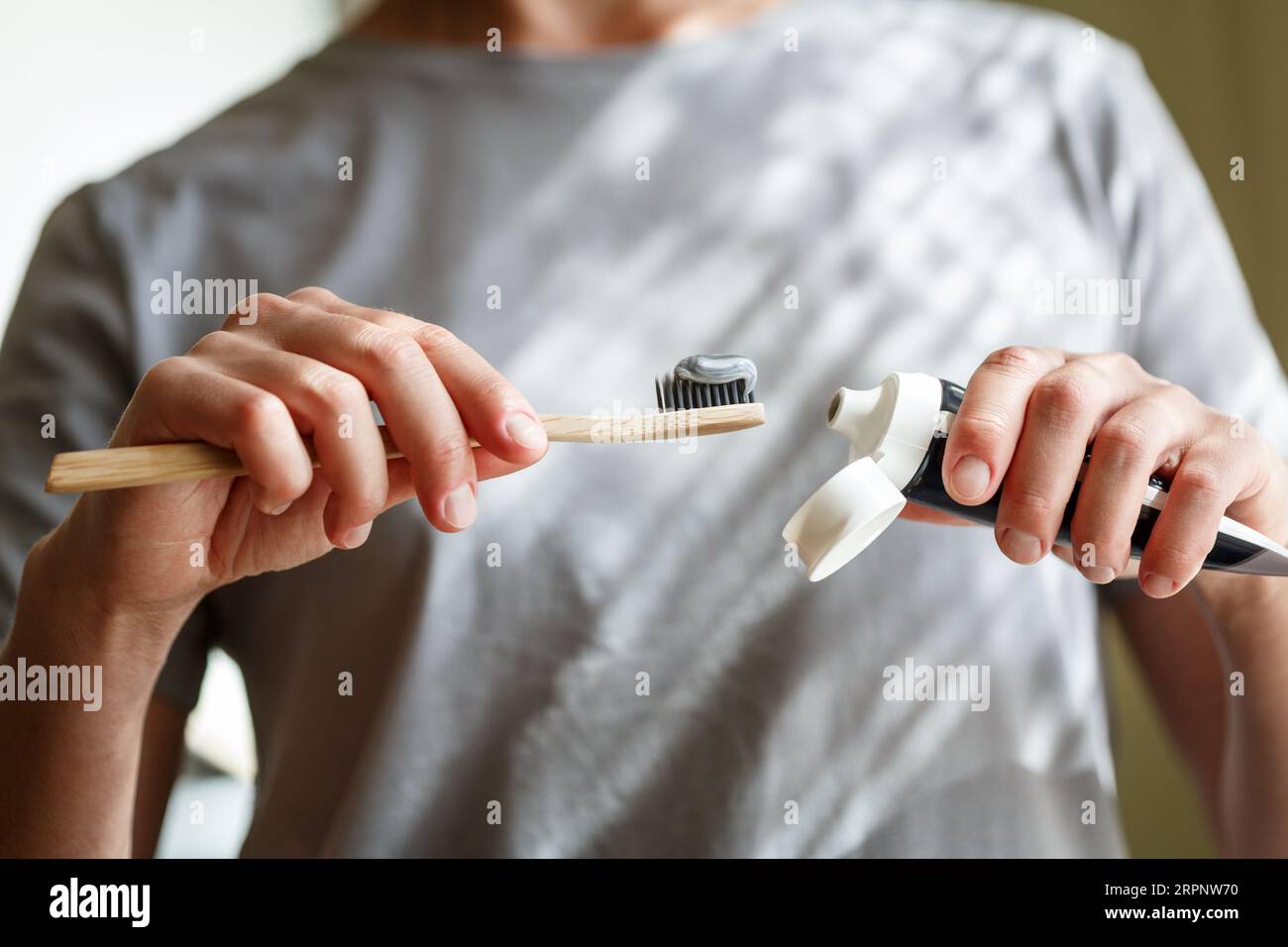 Applying toothpaste on a bamboo tooth brush. Hands squeezing tube with ...