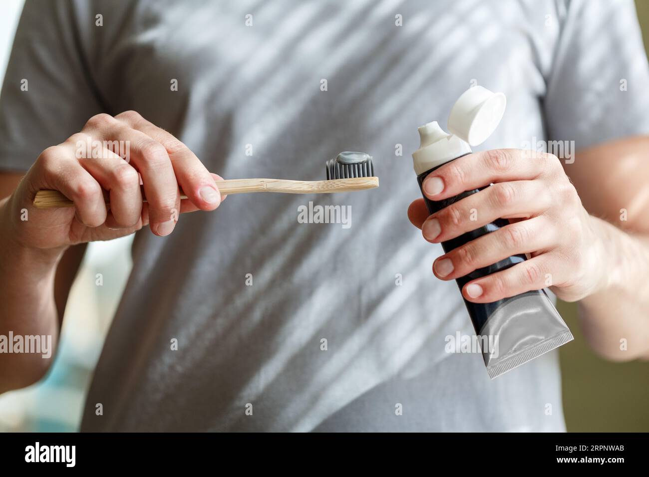 Applying toothpaste on a bamboo tooth brush. Hands squeezing tube with ...