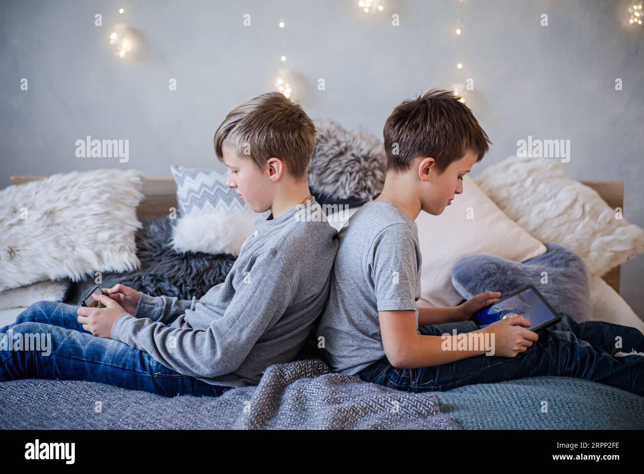 Two boys sitting with their backs turned to each other and playing ...