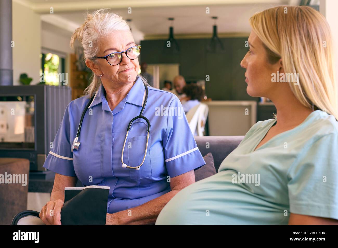 Senior Midwife Visiting Pregnant Woman At Home Taking Blood Pressure ...