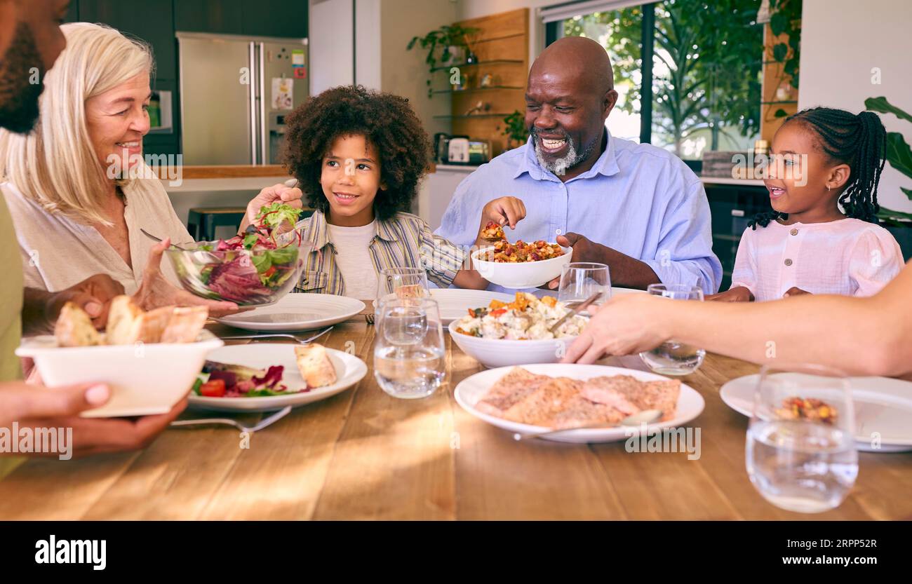 Multi-Generation Family Sitting Around Table Serving Food For Meal At ...