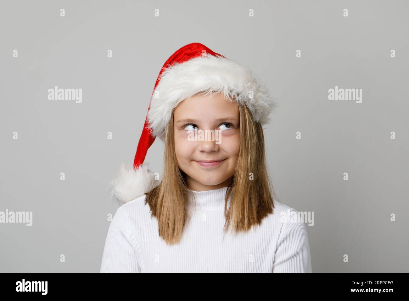 Cute mischievous child girl in Santa hat looking up on white background ...
