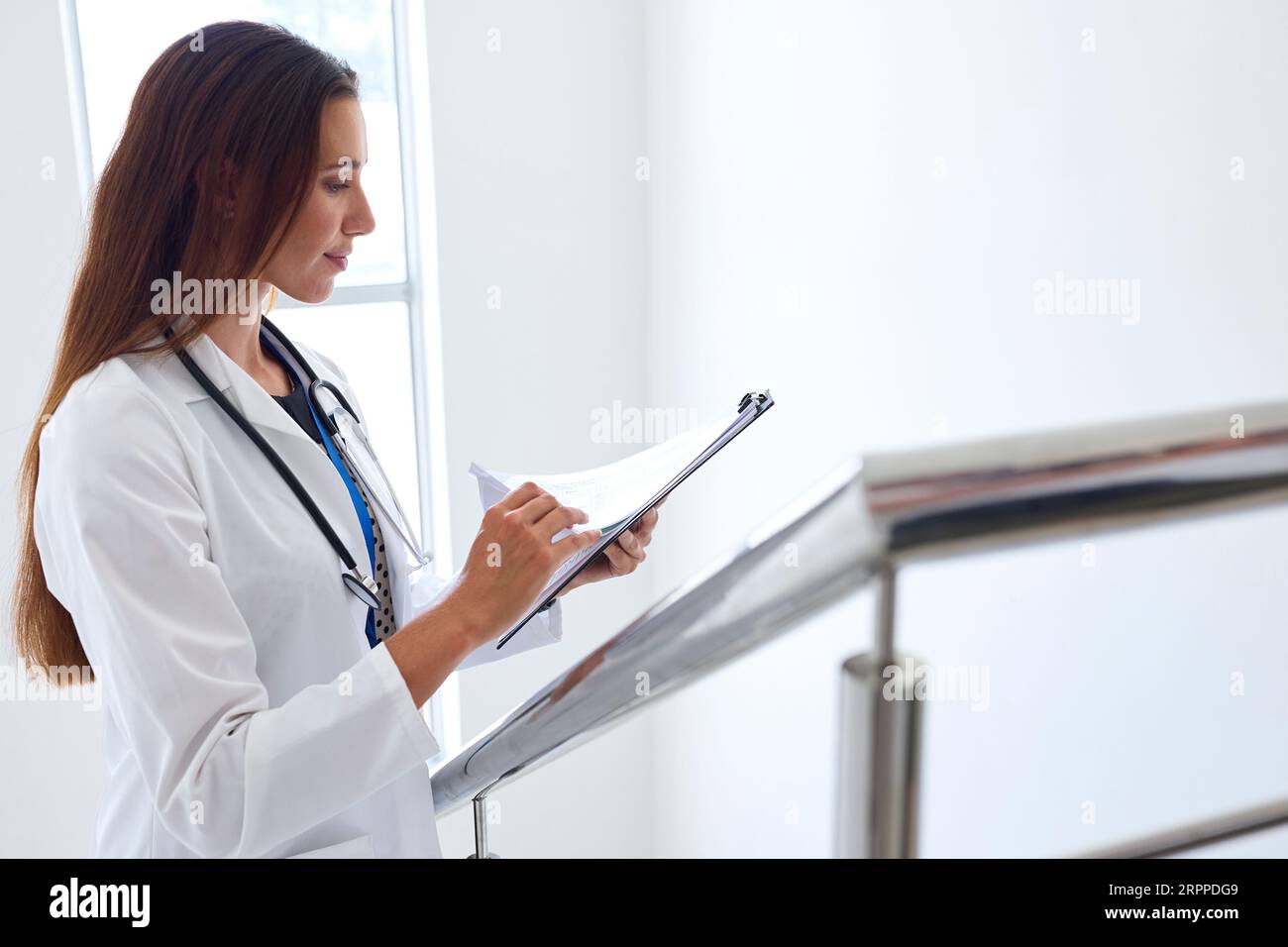 Female Doctor With Clipboard Checking Patient Notes On Stairs In ...
