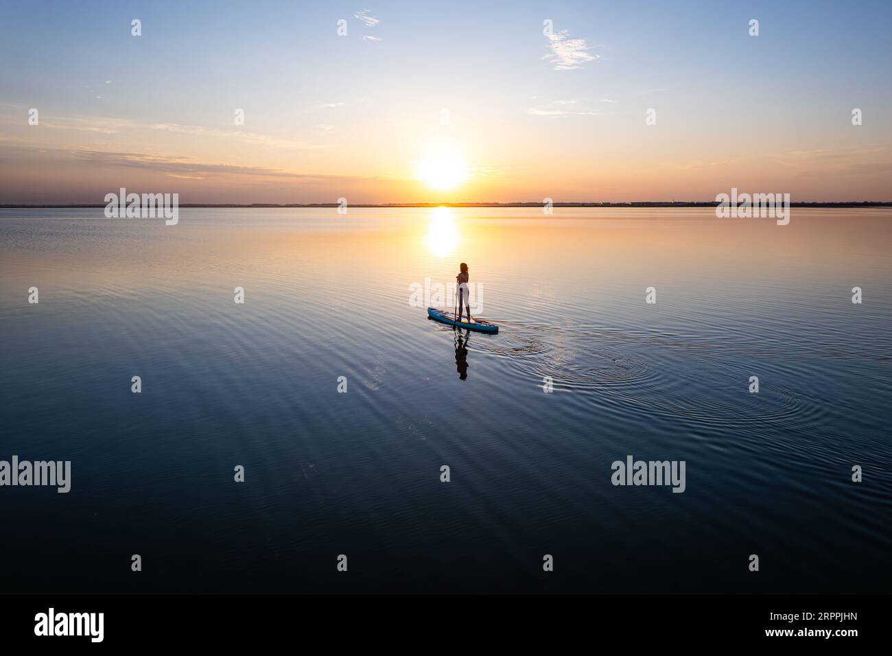 Girl paddling on SUP board on beautiful lake during sunset or sunrise ...