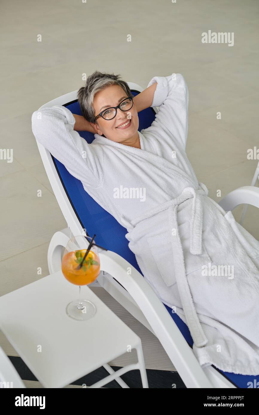 retreat concept, happy mature woman in white robe resting on lounger ...