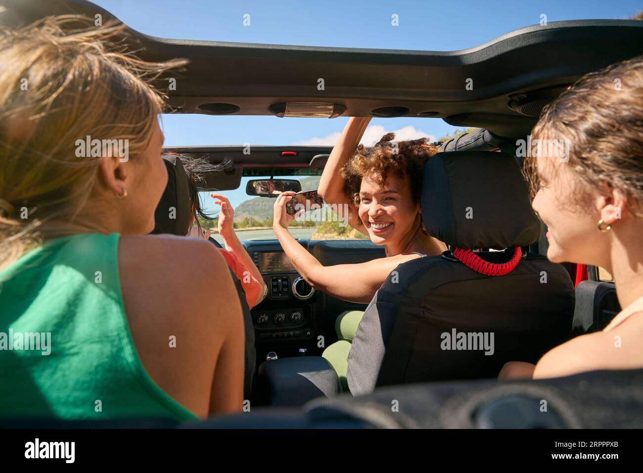 Group Of Laughing Female Friends Having Fun In Open Top Car On Road ...