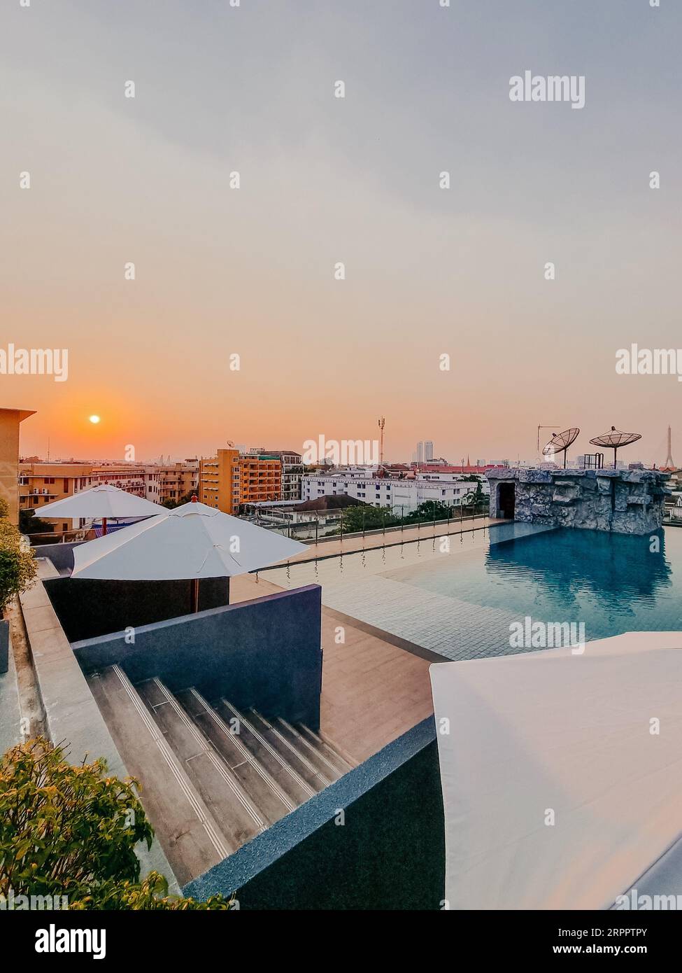 A stunning orange sunset is visible behind a pristine swimming pool ...
