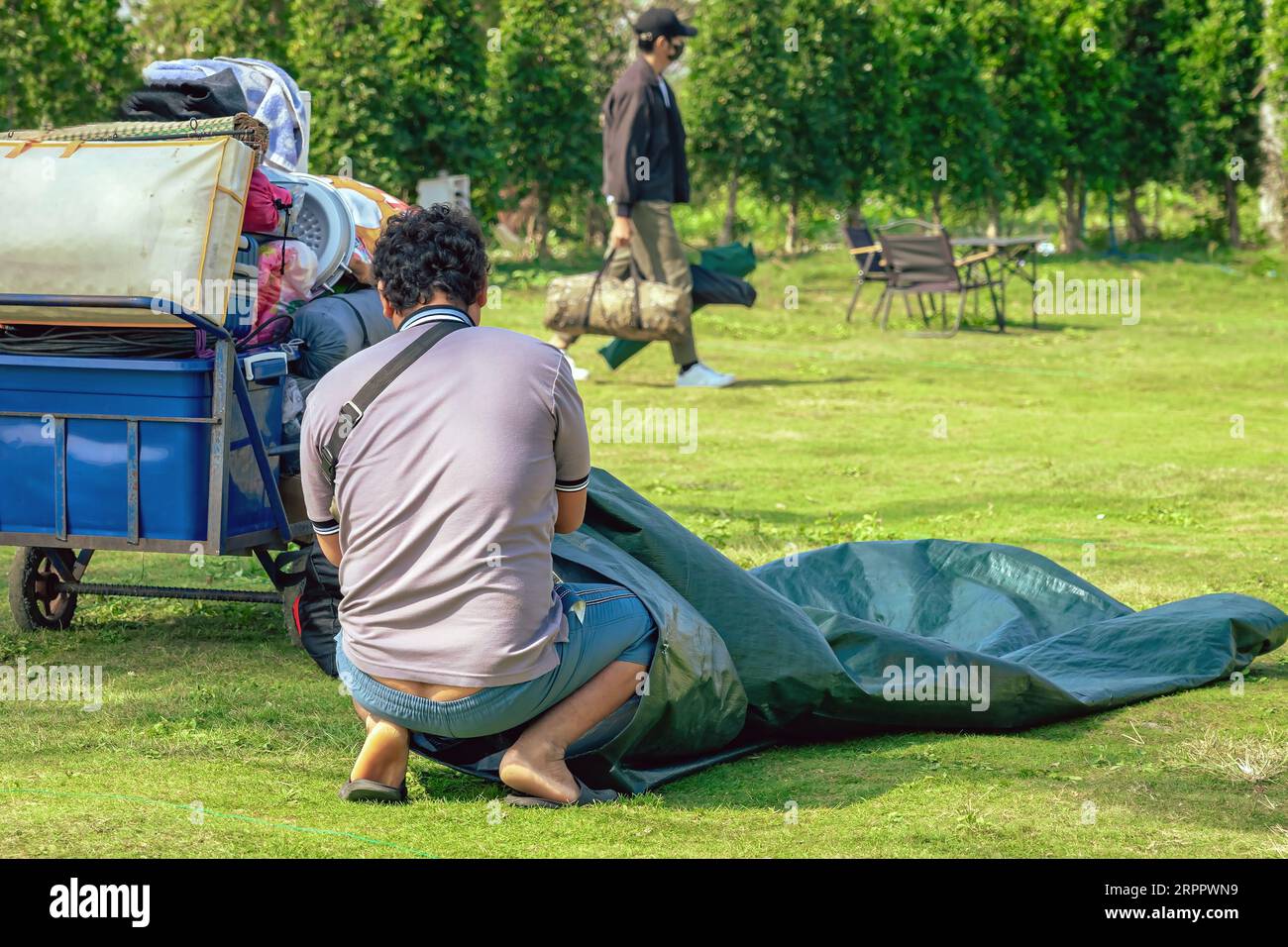 Back view of Asian man clean and collect tarps used to set up their ...
