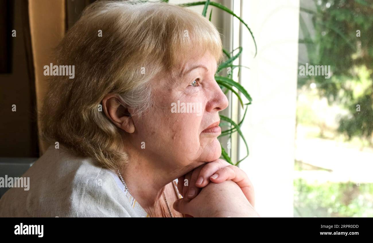 Happy smiling old woman looking out the window and wating to someone ...