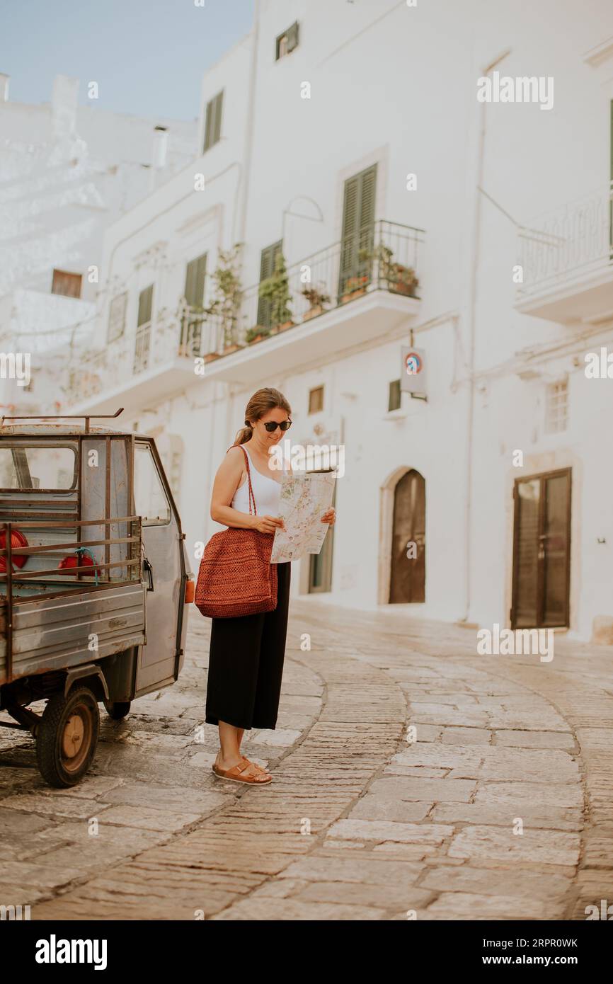 Female tourist with a paper city map on narrow streets of Ostuni, Italy ...