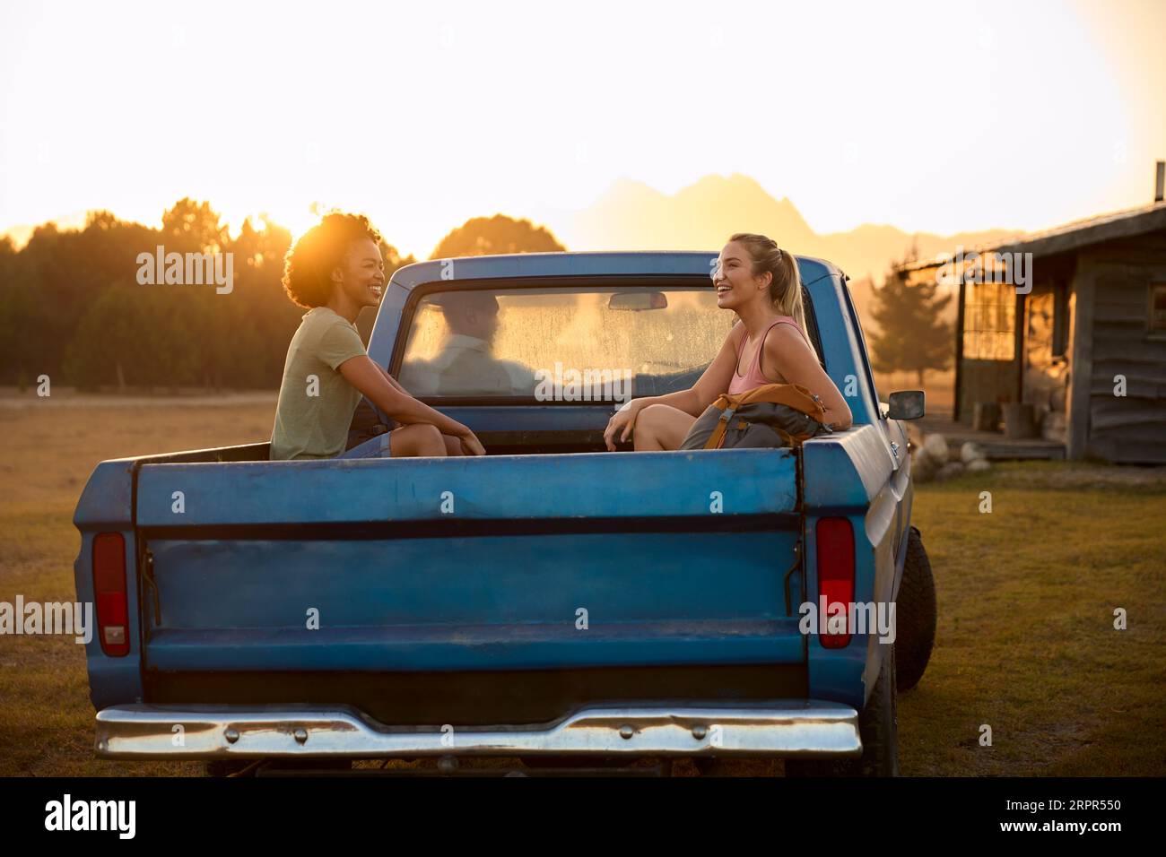 Two Women Riding In Back Of Pick Up Truck As Friends Arrive At ...