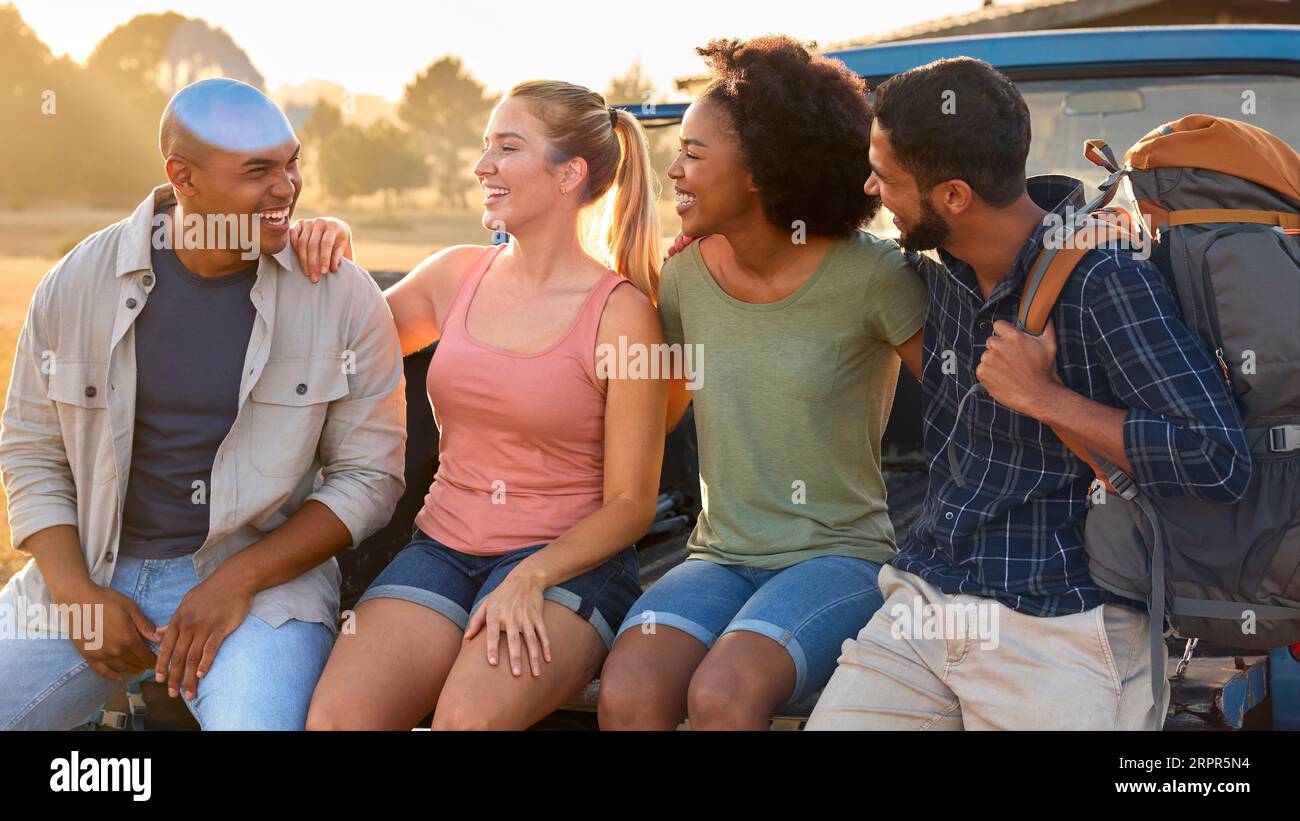 Group Of Friends Sitting On Tailgate Of Pick Up Truck On Road Trip To ...