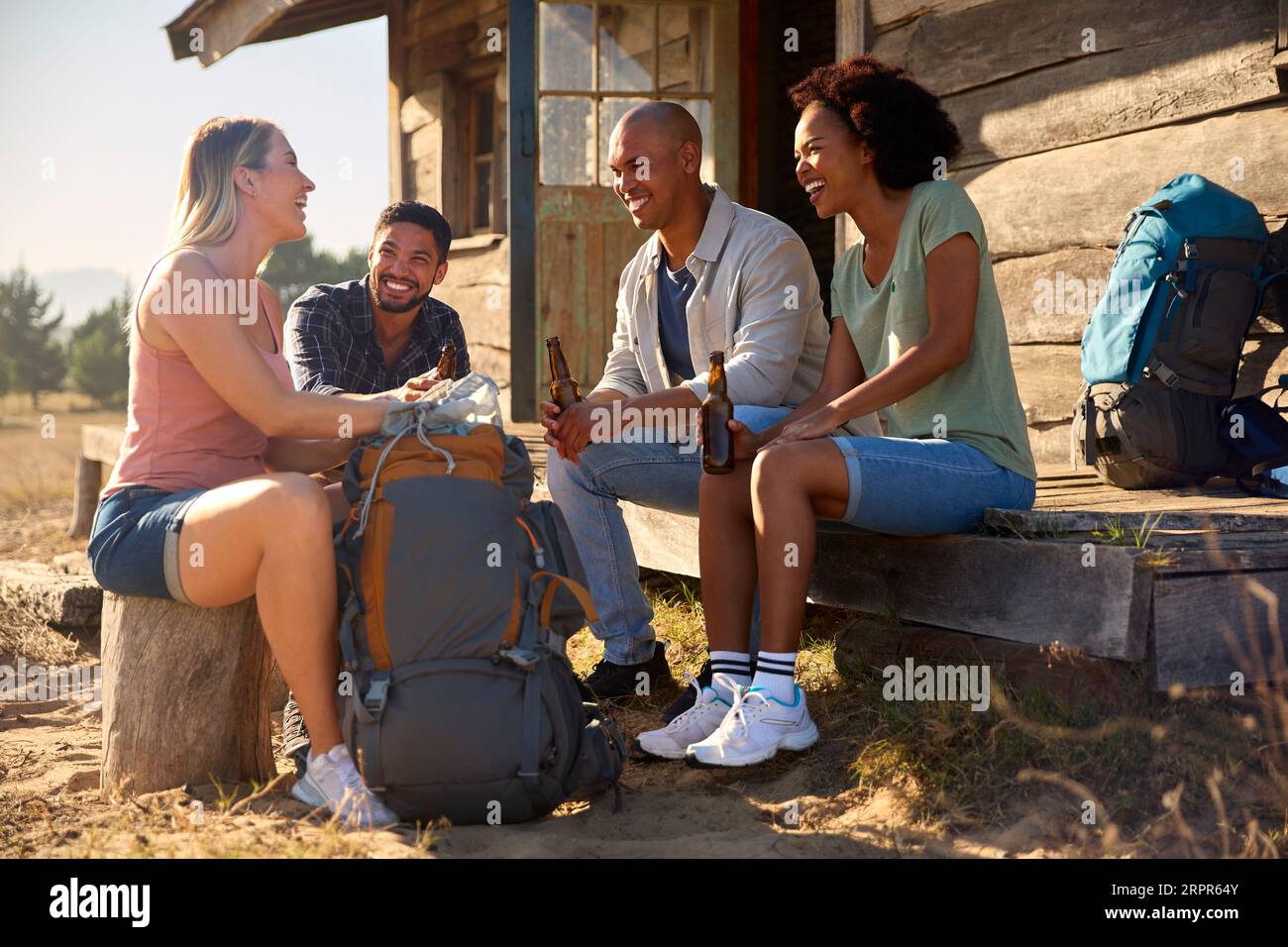 Group Of Friends On Vacation Sitting On Porch Of Countryside Cabin ...