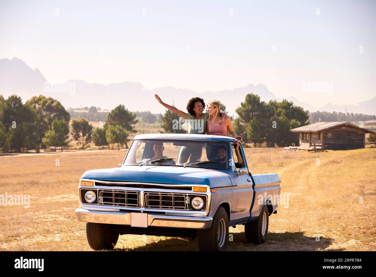 Two Women Standing In Back Of Pick Up Truck As Friends Enjoy Road Trip ...