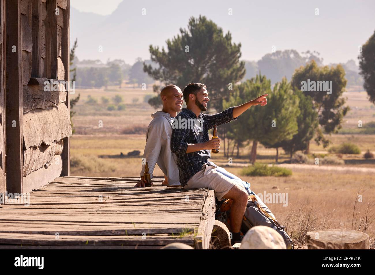 Two Male Friends On Vacation Sitting On Porch Of Countryside Cabin ...