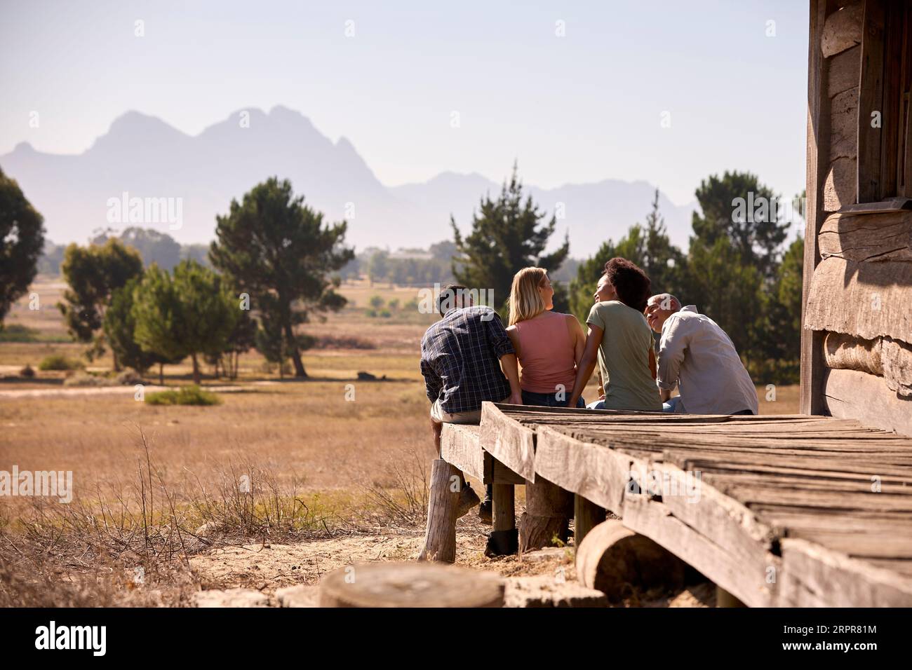 Rear View Of Group Of Friends On Vacation Sitting On Porch Of ...