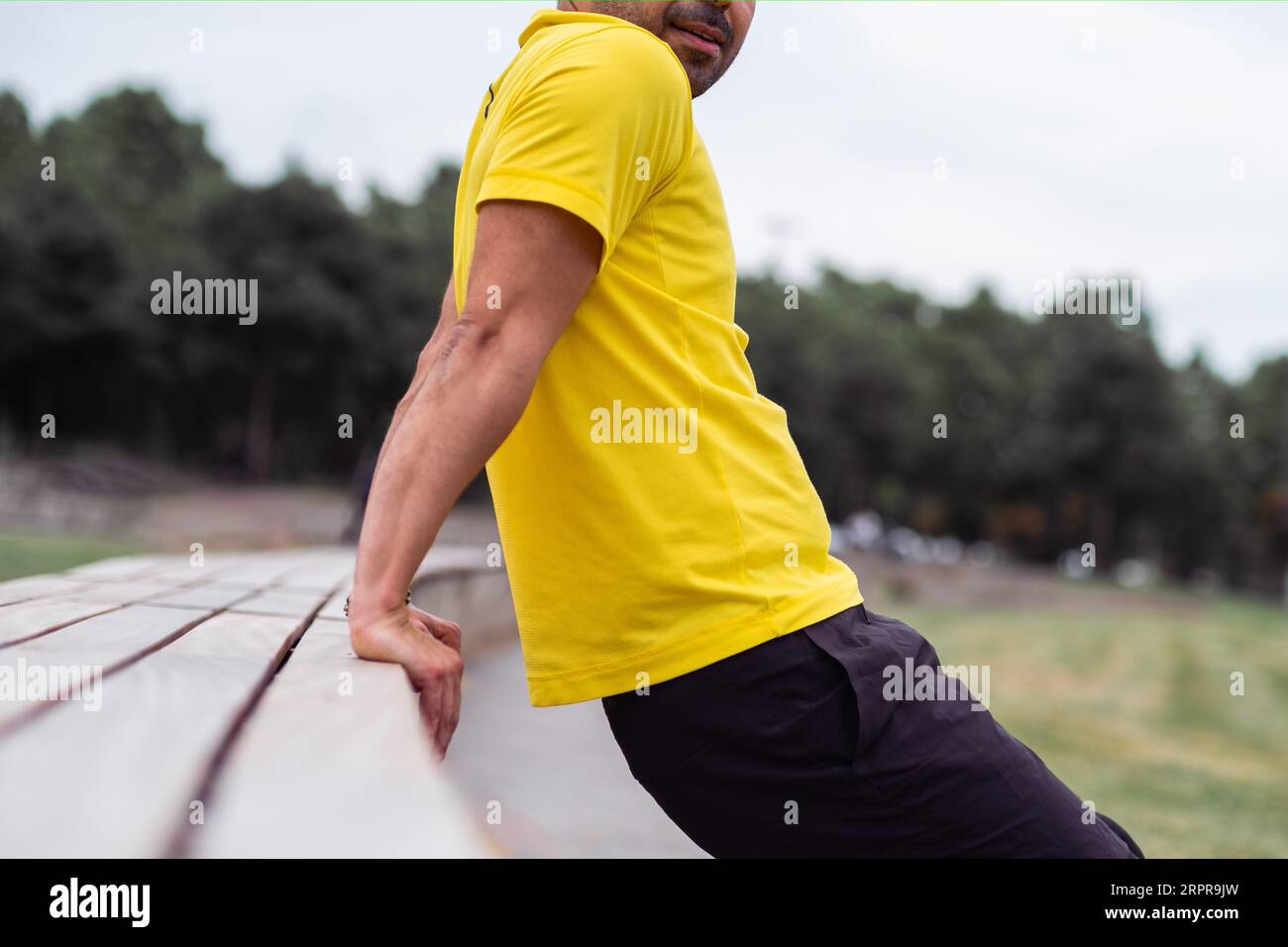 working on arm muscles, man in yellow t-shirt performs backward push ...