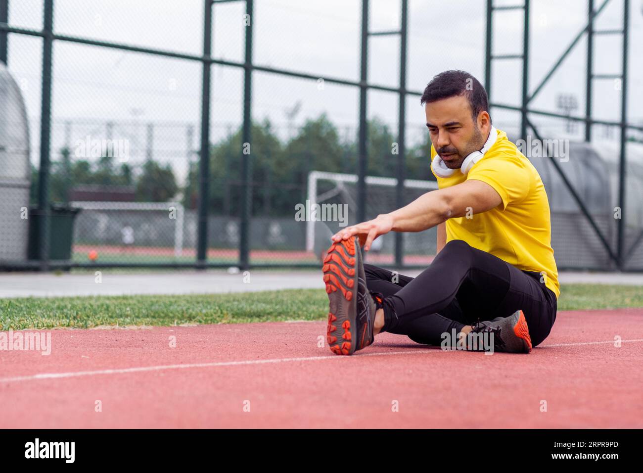 Athlete with headphones touching foot toes sitting on running track at ...