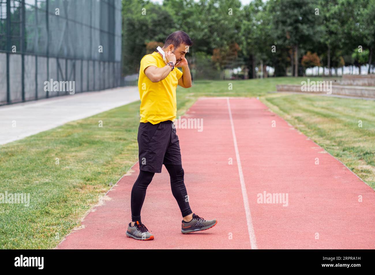 Man in tracksuit putting on cordless earphones walking along track at ...