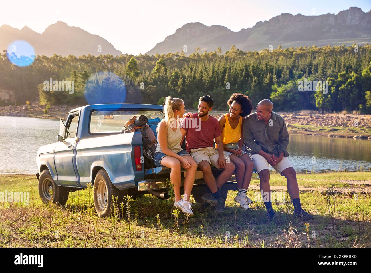 Group Of Friends With Backpacks In Pick Up Truck On Road Trip By Lake ...