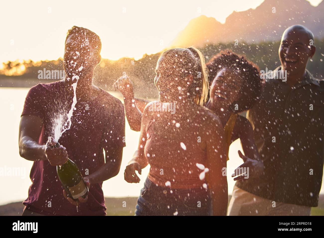 Group Of Friends Celebrating Outdoors By Lake Opening And Spraying ...