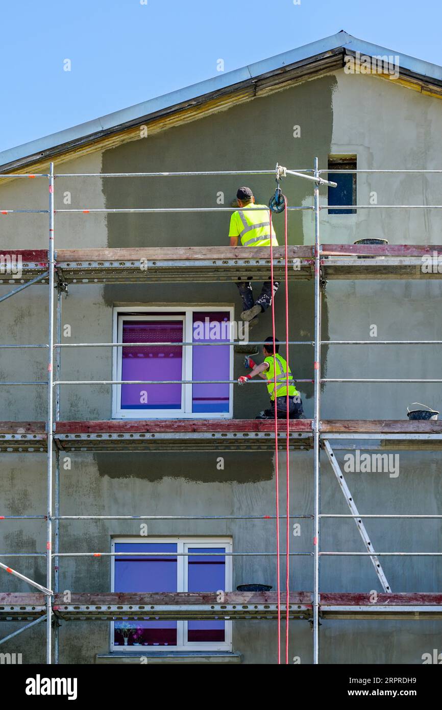 Two painters in green safety vests paint the facade of a residential ...
