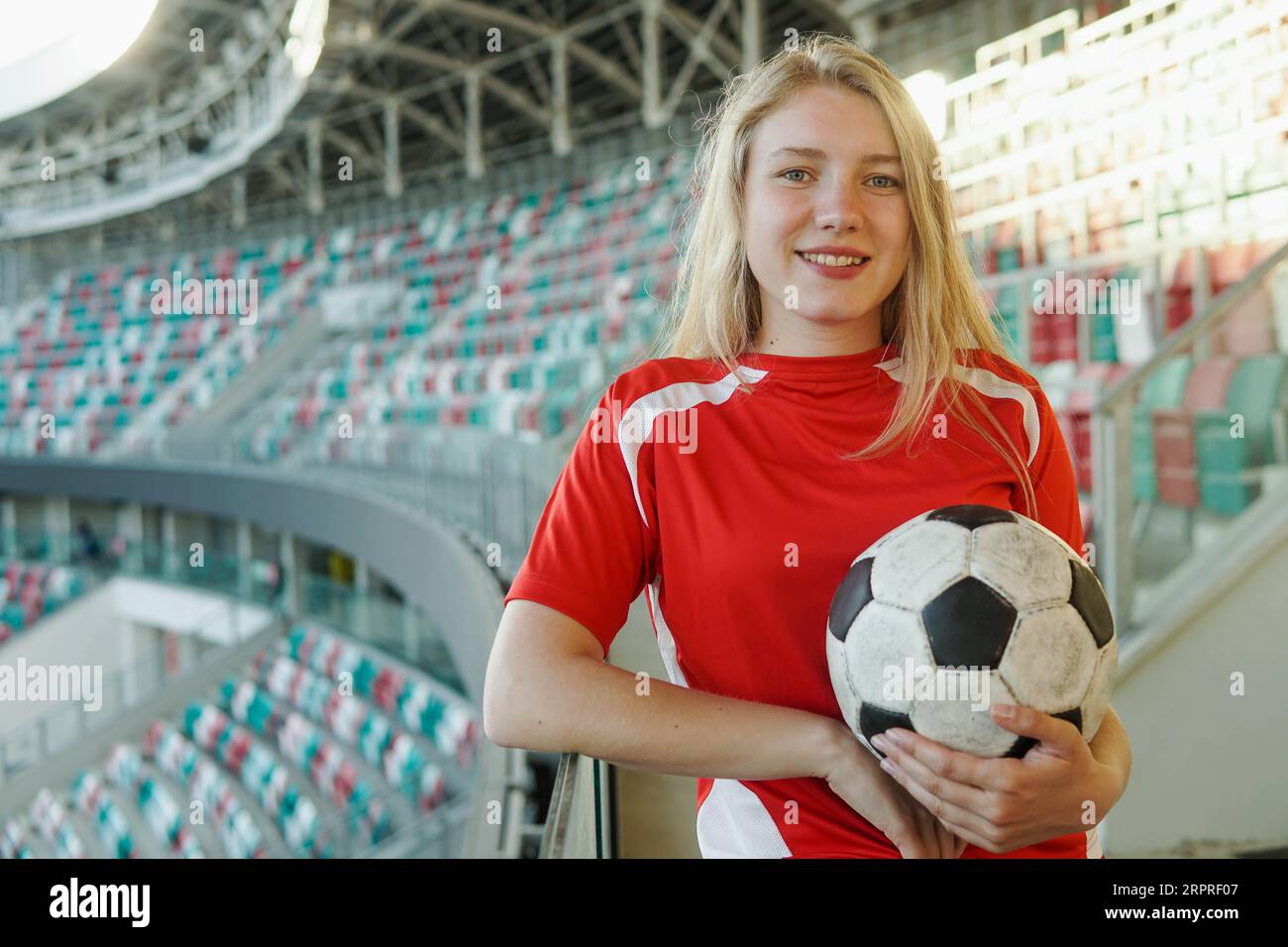 Portrait of young caucasian woman in red football strip holding ball at ...