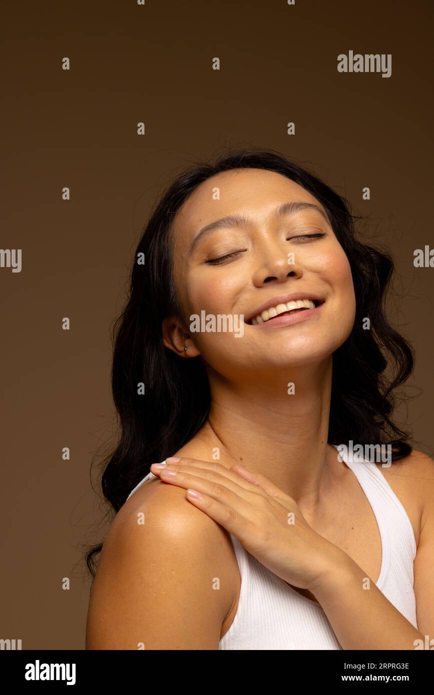 Happy asian woman with dark hair, with hand on shoulder and eyes closed ...