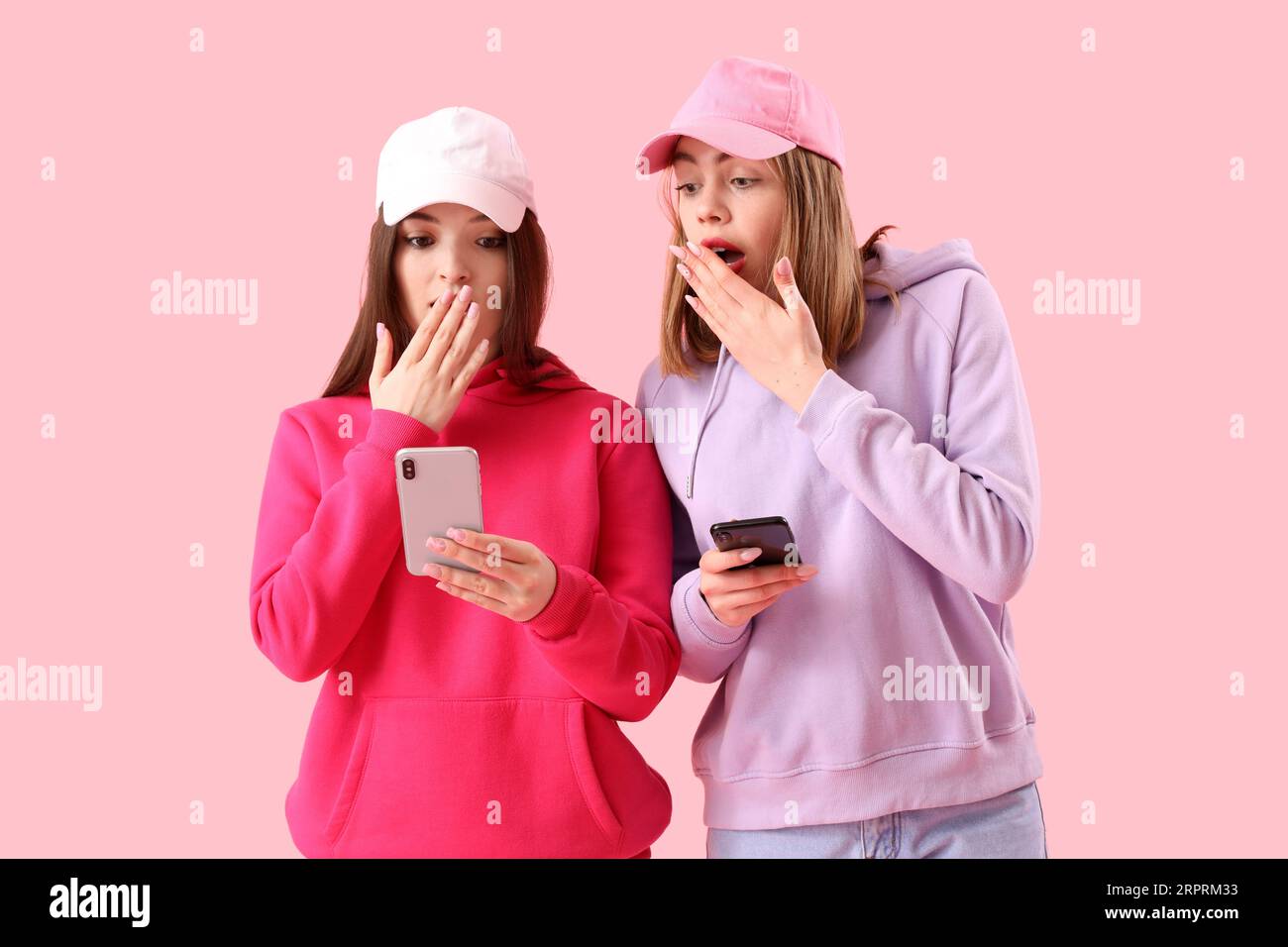 Shocked female friends using mobile phones on pink background Stock ...