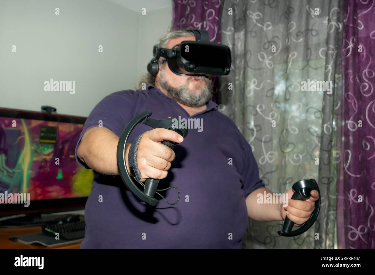 Overweight man playing virtual reality raising hands with joysticks at ...