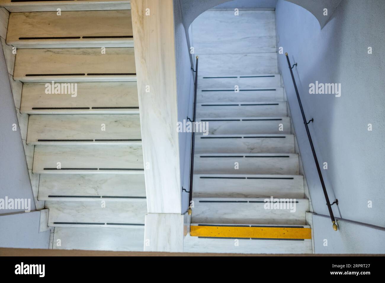 An empty white staircase in an old building with a single yellow ...