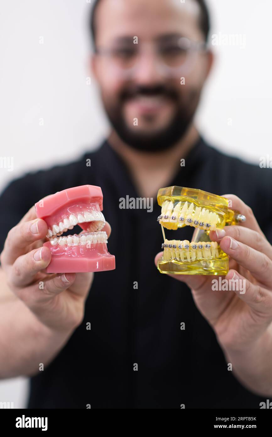 Smiling orthodontist holding plastic human jaws models with metal ...