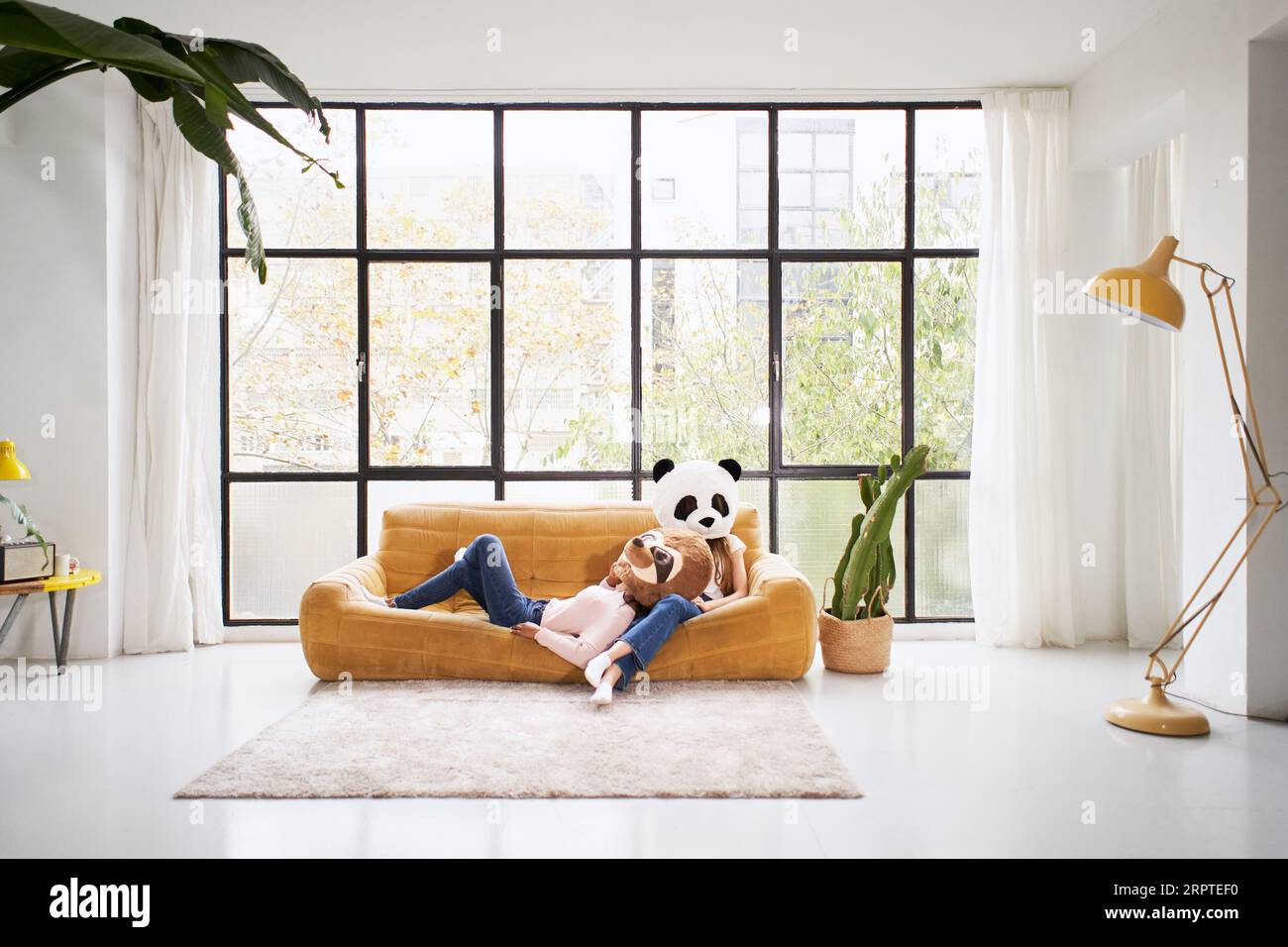 Unrecognizable female couple lying on sofa giant panda bear and sloth ...
