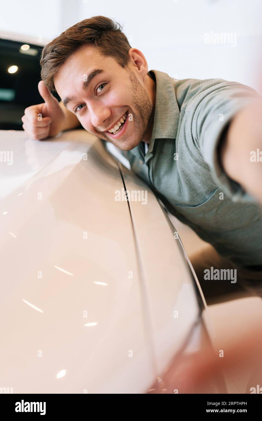 Vertical Portrait Of Cheerful Buyer Male Hugging Stroking Car Hood After Purchased In