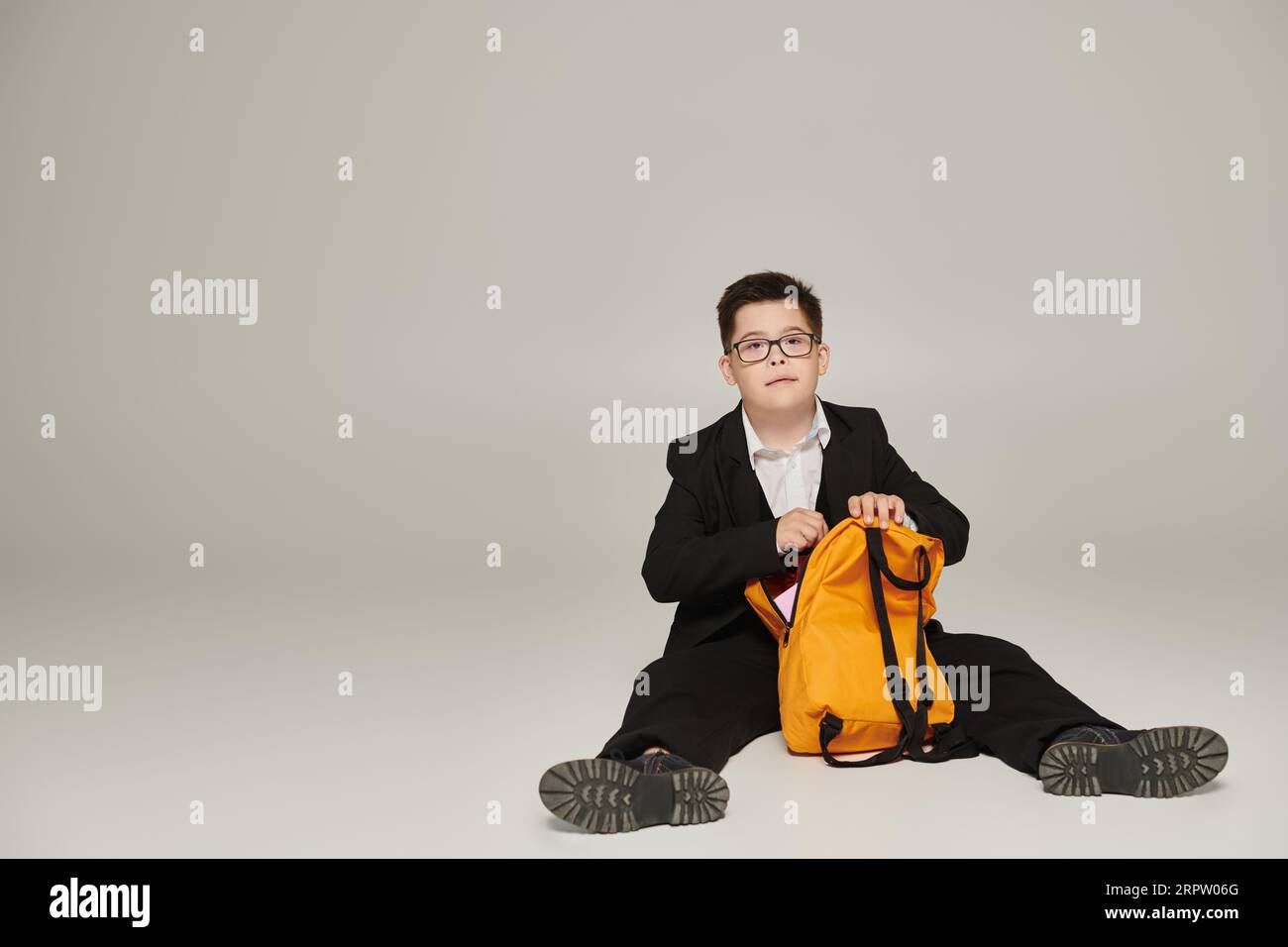 kid with down syndrome in school uniform sitting with yellow backpack ...