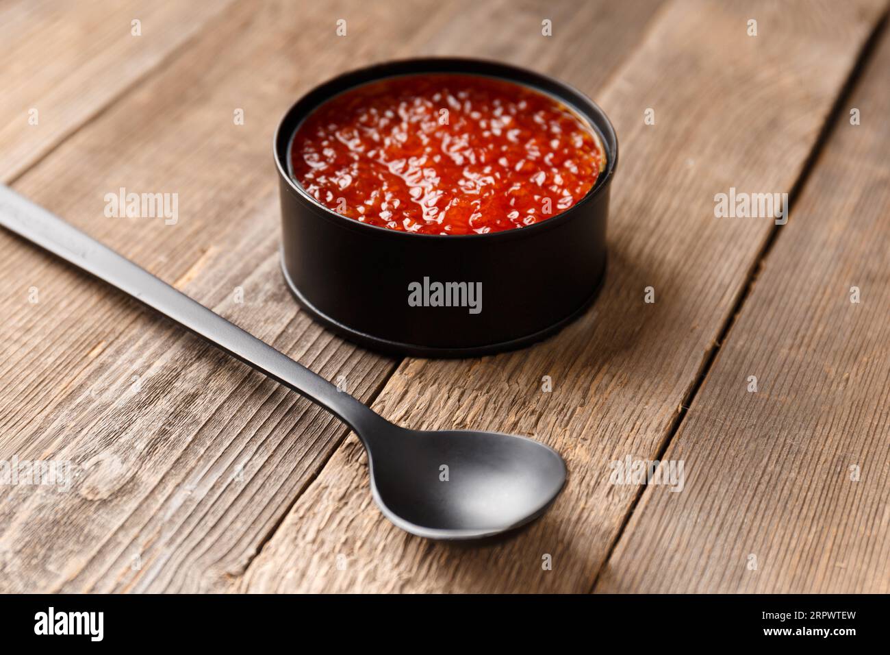 Red salmon caviar in an open black tin can and a black spoon on wooden ...