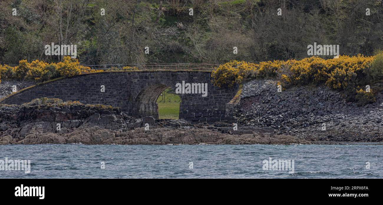 Sturdy old stone bridge where a river leads into a sea loch covered in ...