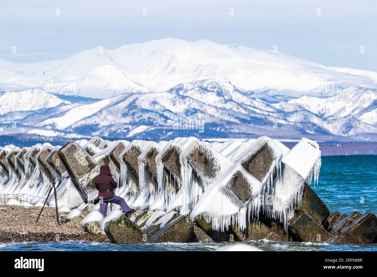 Tourist takes images of ice covered concrete wave breakers on the ...