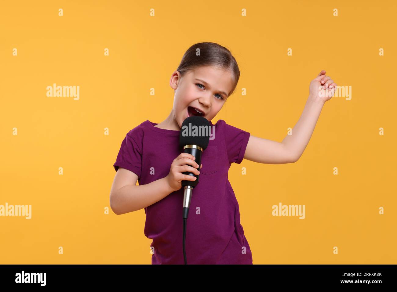 Cute little girl with microphone singing on yellow background Stock ...