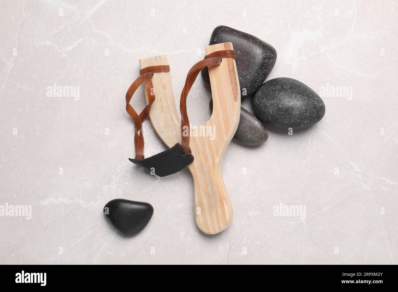 Wooden slingshot with stones on light grey marble background, flat lay ...