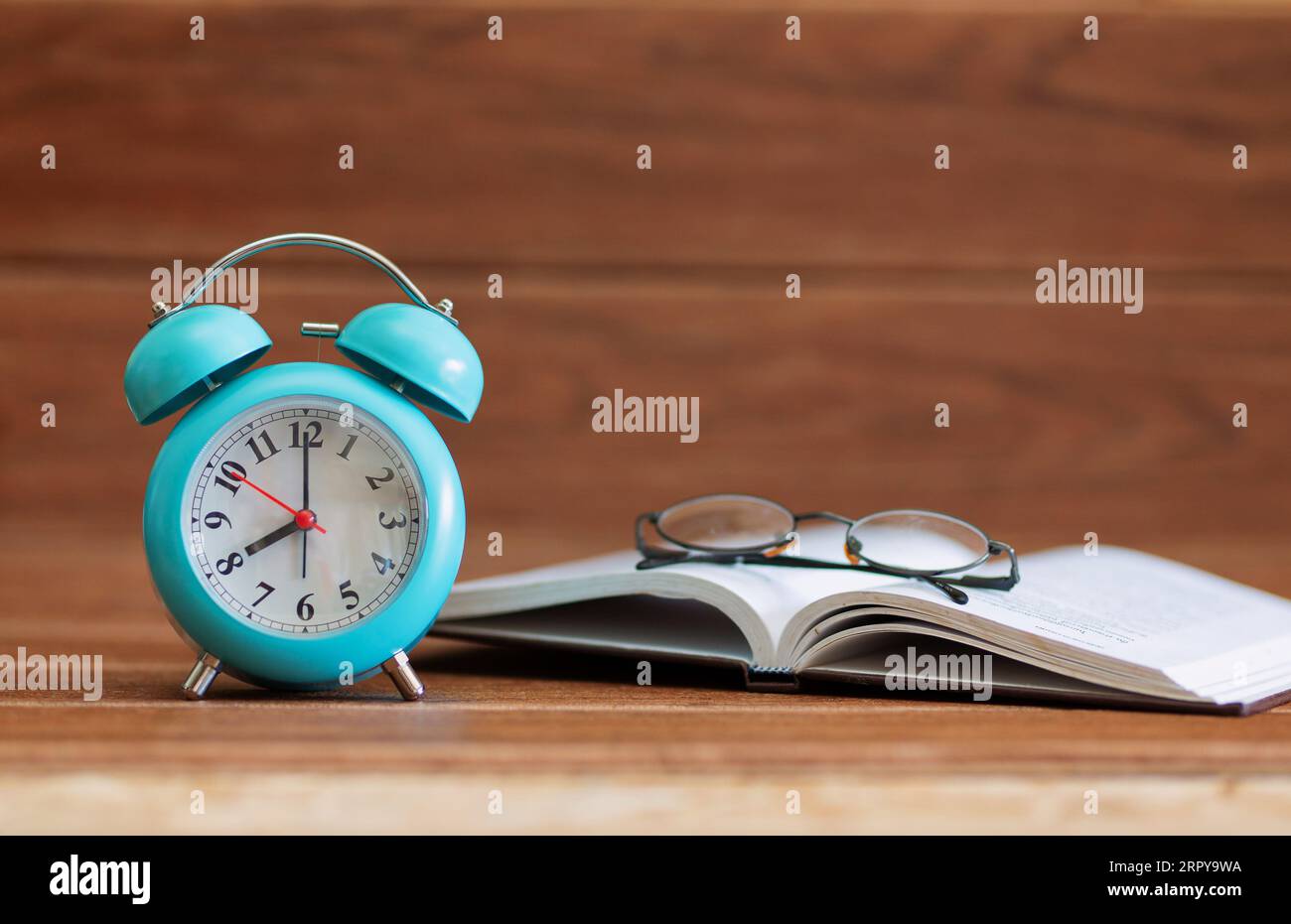 Colorful alarm clock, books, glasses on wooden table on wood grain ...