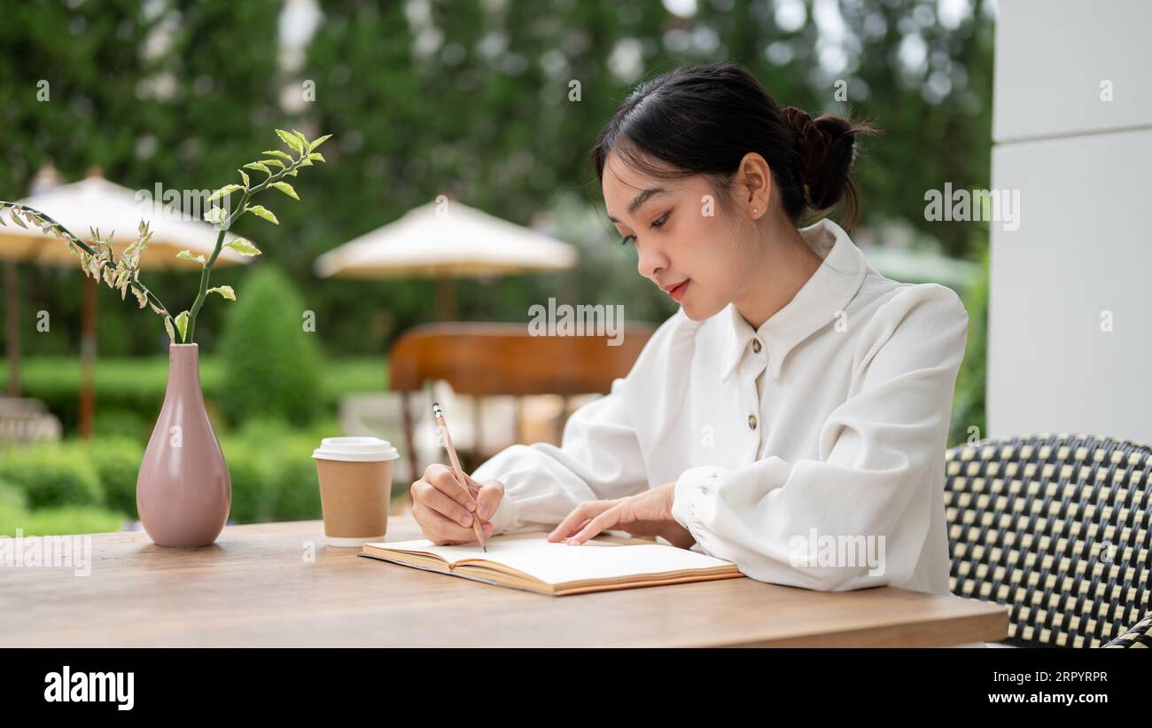 A beautiful young Asian woman is writing something in her notebook ...