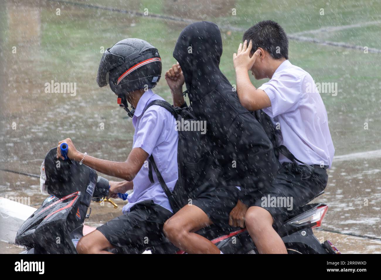A group of students ride a motorcycle in the rain, Bangkok, Thailand ...