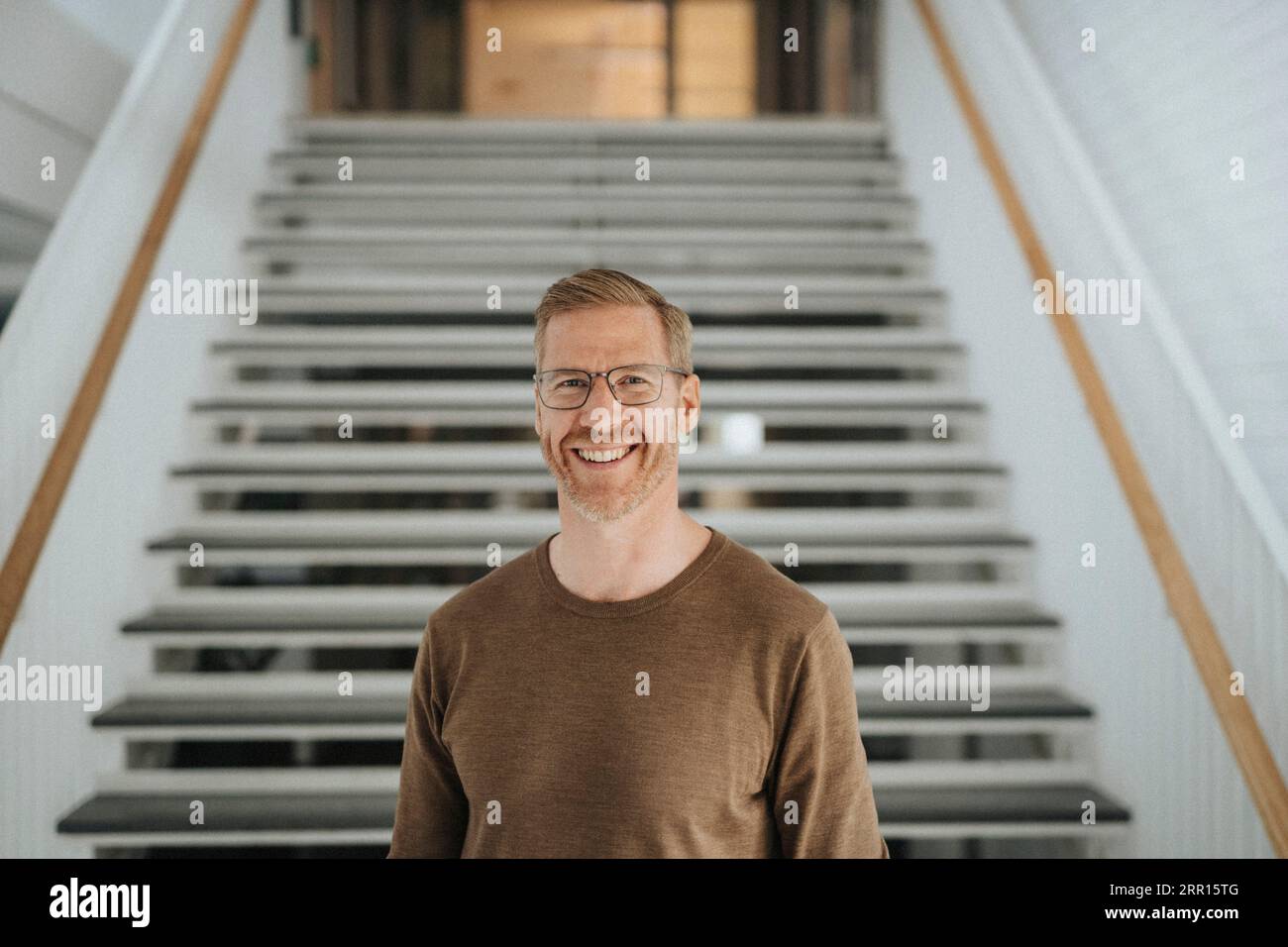 Portrait of happy mature professor standing against steps in university ...