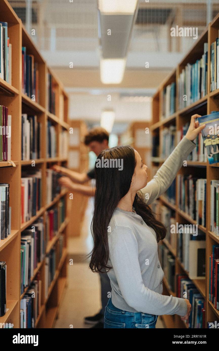 Side view of female student searching books on bookshelf in library at ...